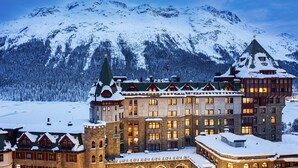 Um hotel histórico com vários edifícios, uma torre imponente e uma paisagem montanhosa coberta de neve.