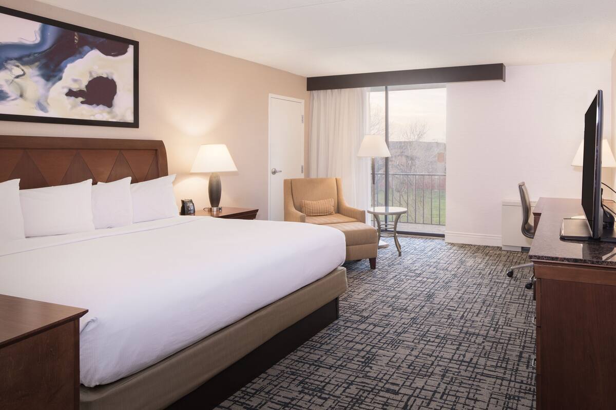 Quarto de hotel com uma cama grande, uma cadeira, uma mesa e uma televisão.