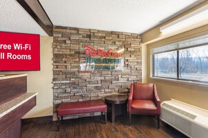 Recepção do Red Roof Inn com parede de pedra, um banco, uma cadeira e uma janela com vista.