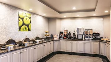 Uma cozinha moderna com armários brancos, bancadas de granito e diversos eletrodomésticos, incluindo cafeteira, máquina de waffles e distribuidores de alimentos.