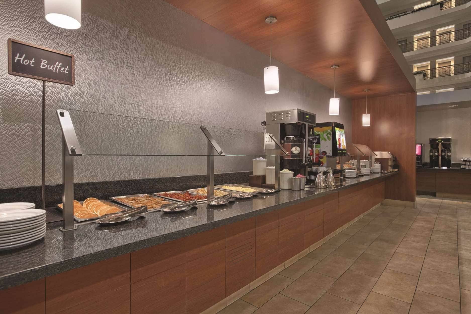 Uma área de buffet com um letreiro indicando "Hot Buffet", diversos tabuleiros de comida e uma máquina de café.