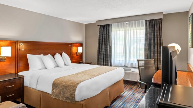 Quarto de hotel com cama grande, escrivaninha, cadeira e televisão.