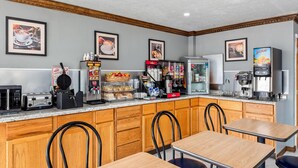 Um café com armários de madeira, uma máquina de café, um dispensador de suco e quadros nas paredes.