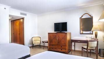 Quarto de hotel com uma cama, uma escrivaninha de madeira, uma televisão, um espelho e uma cadeira.