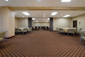 Sala de conferência com mesas e cadeiras, piso coberto de carpete e uma parede lisa com uma porta.