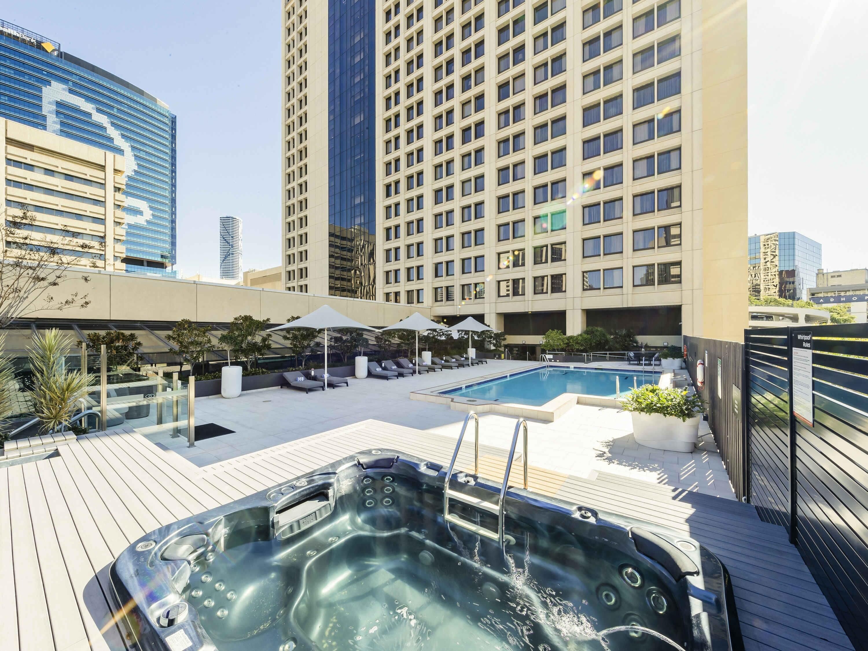 Uma área de piscina no terraço com hidromassagem, espreguiçadeiras e guarda-sóis.