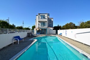 Um edifício moderno com piscina, área coberta e um muro branco com grade.