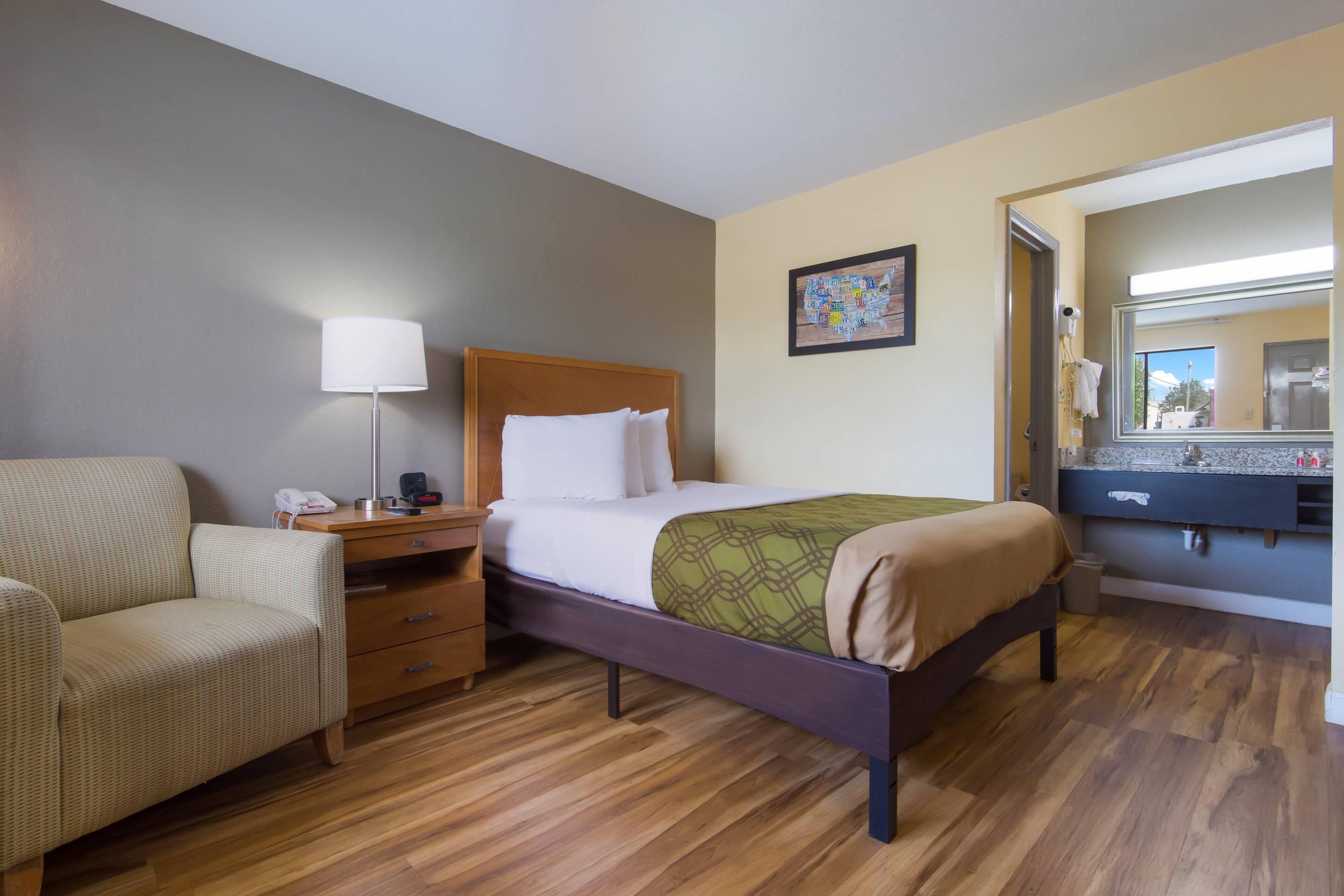 Quarto de hotel com cama, cadeira, mesa de cabeceira, luminária, espelho e mapa fixado na parede.