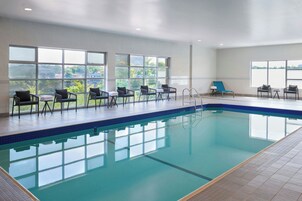 Piscina interna com vista ampla por grandes janelas, cercada por espreguiçadeiras e um deck revestido em azulejos azuis.