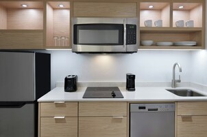 Uma cozinha moderna com micro-ondas embutido, torradeira e cafeteira na bancada, máquina de lavar louça e armários de madeira.