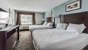 Quarto de hotel com duas camas, uma escrivaninha e uma janela com cortinas.