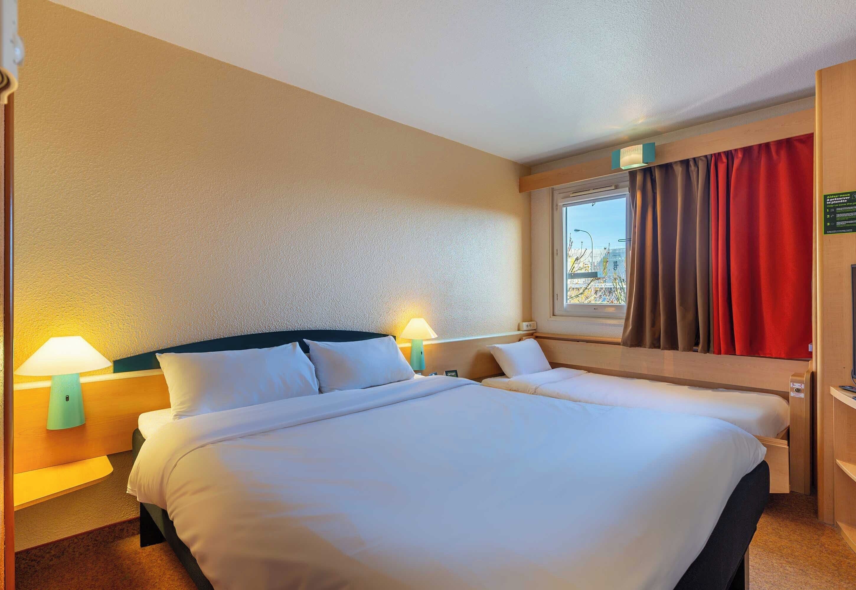 Quarto de hotel com duas camas, janela com cortinas e vista para a cidade.
