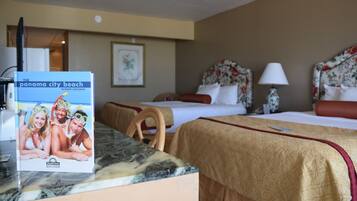 Quarto de hotel com cama, escrivaninha com computador, cadeira, abajur e quadro na parede.