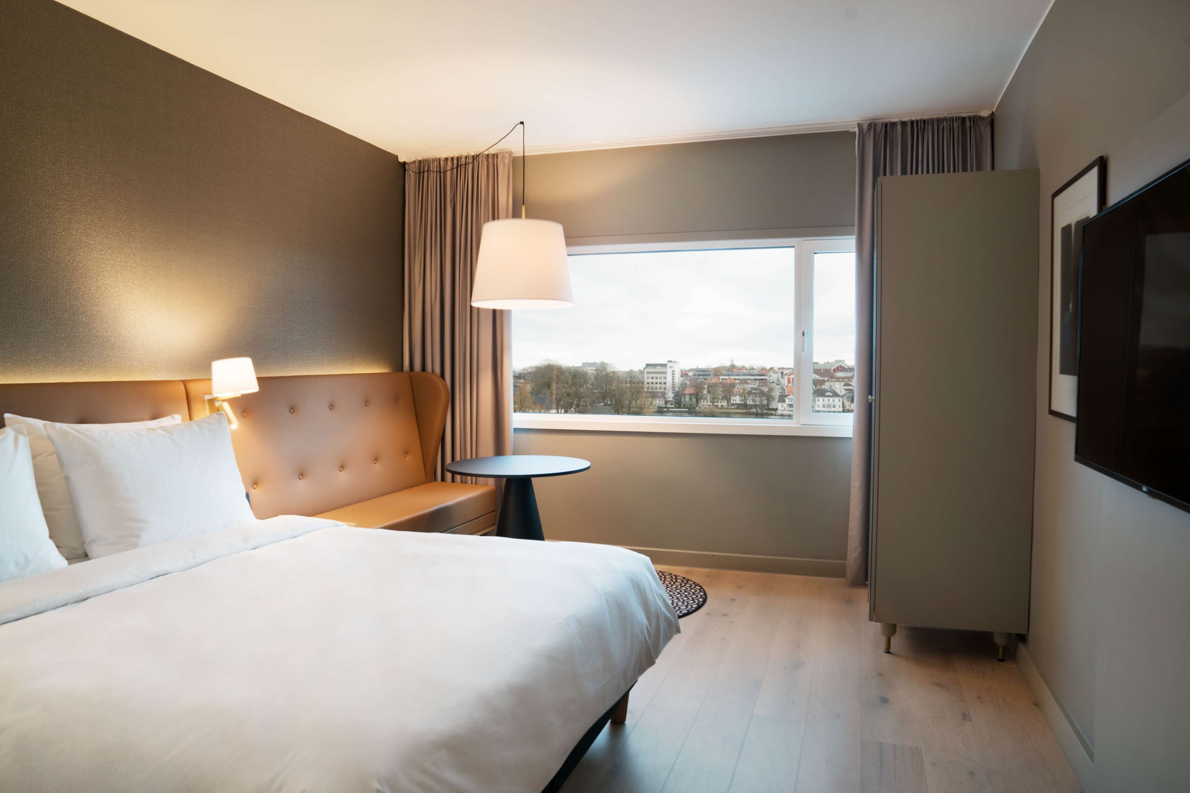 Quarto de hotel com uma cama grande, uma mesa pequena, televisão e janela com vista para a cidade.