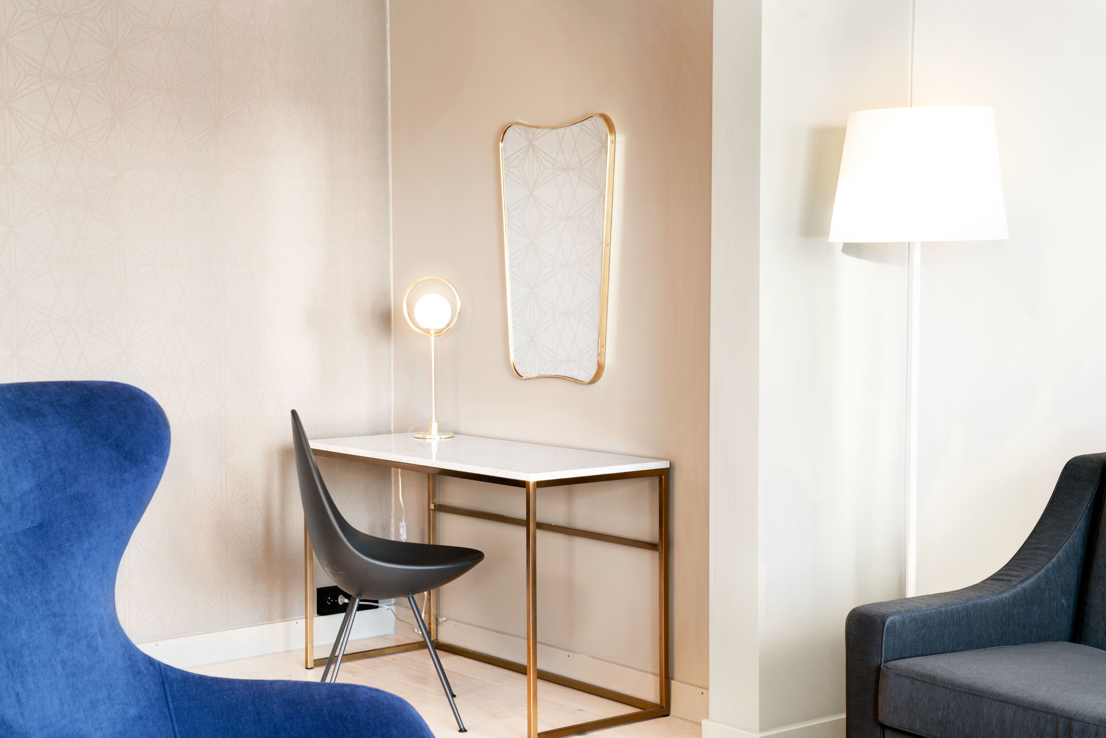 Quarto moderno com escrivaninha, duas cadeiras, luminária de parede e um espelho decorativo.