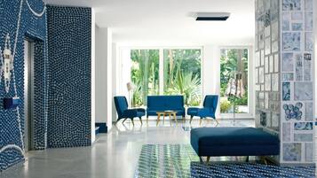 Uma sala de estar moderna com um sofá azul, duas poltronas e uma mesa de centro. Há uma janela grande com vista para o verde lá fora.
