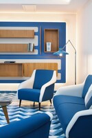 Uma sala de estar moderna com mobiliário azul e branco, piso com padrão geométrico e estantes em madeira com livros.