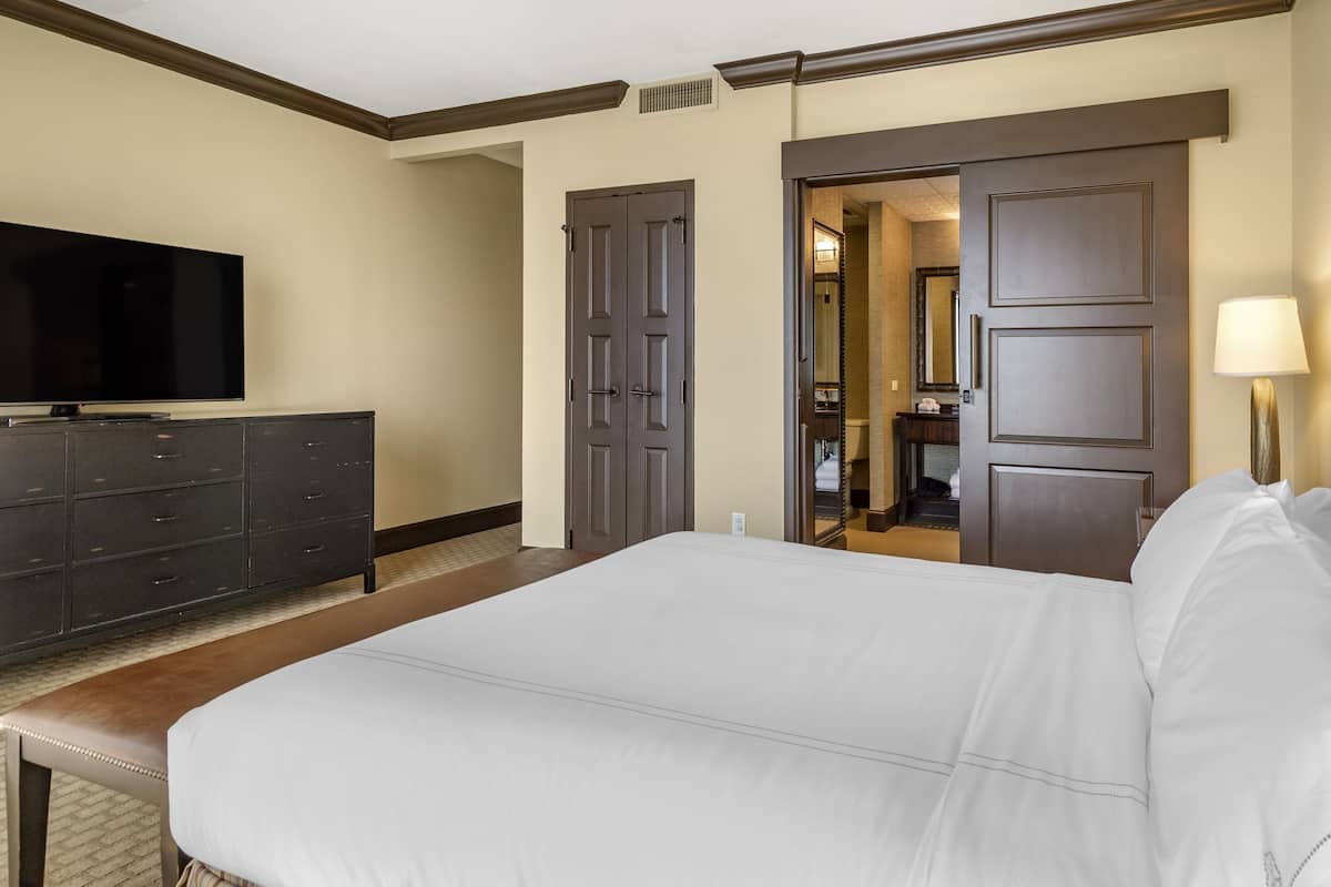 Quarto de hotel com uma cama grande, cômoda, televisão e porta que dá para um banheiro.