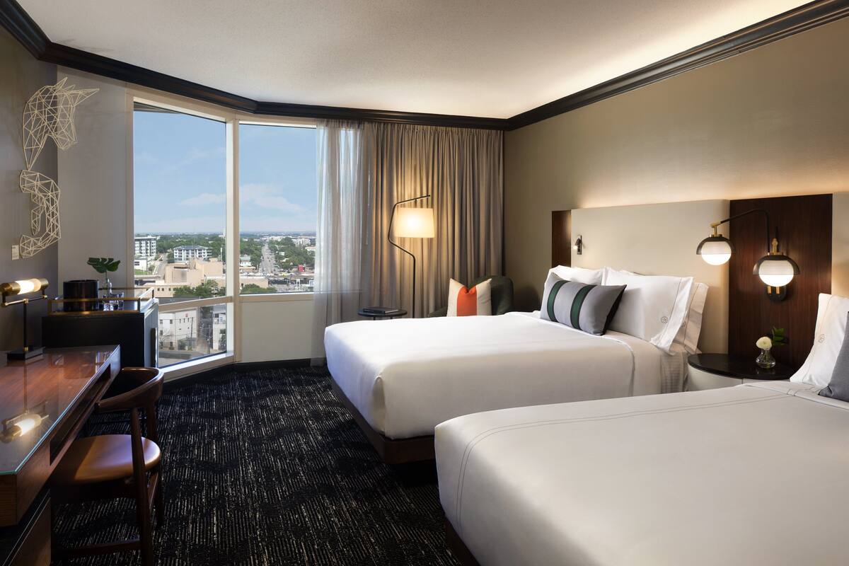 Quarto de hotel com duas camas, uma escrivaninha e vista para a cidade.