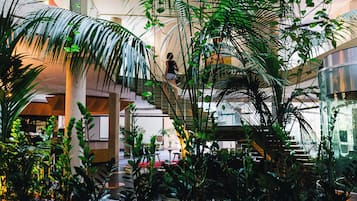 Um amplo átrio interno com uma escadaria central rodeada por vegetação exuberante e arquitetura moderna.
