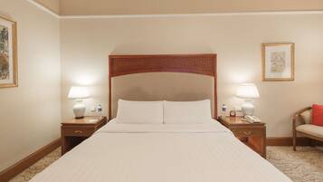 Quarto de hotel com uma cama grande, duas mesas de cabeceira com abajures, uma cadeira e um quadro na parede.
