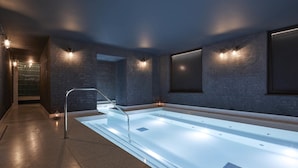 Piscina interior moderna com design minimalista, apresentando borda retilínea, corrimão metálico e iluminação embutida.
