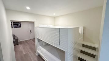 Uma cama beliche com cabeceira, uma porta e uma pequena janela.