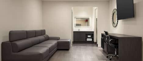 Uma sala de estar moderna com um sofá seccional, uma escrivaninha de madeira escura e uma grande TV de tela plana na parede.