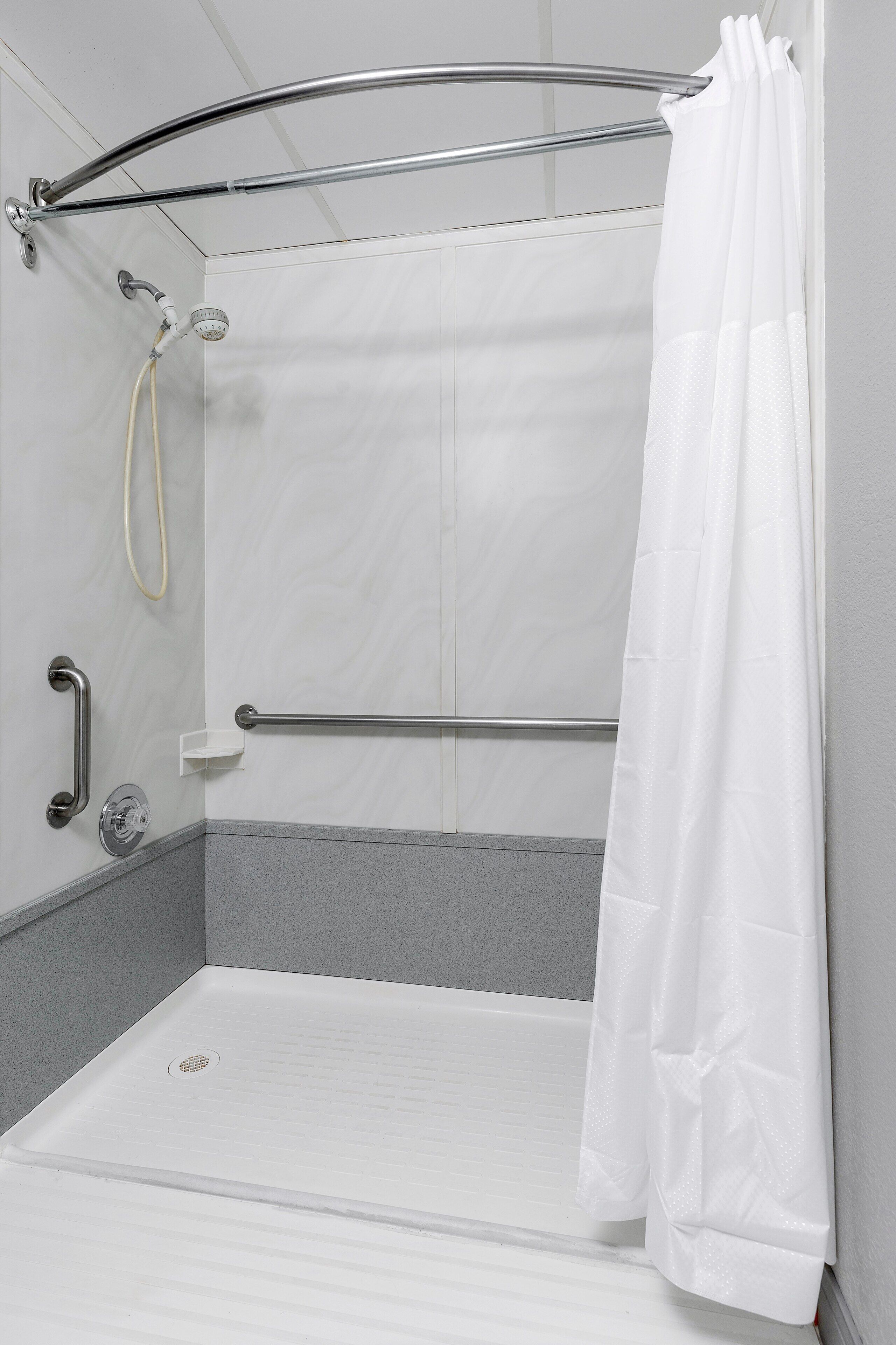 Área de duche com barra de apoio, chuveiro manual e cortina de duche branca.