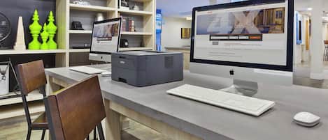 Um escritório moderno com um computador, teclado e rato sobre um balcão. Estantes com diversos objetos e uma cadeira em primeiro plano.