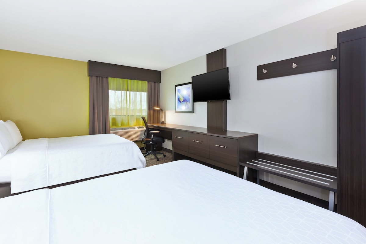 Quarto de hotel com duas camas, uma escrivaninha, uma cadeira, uma televisão e um guarda-roupa.