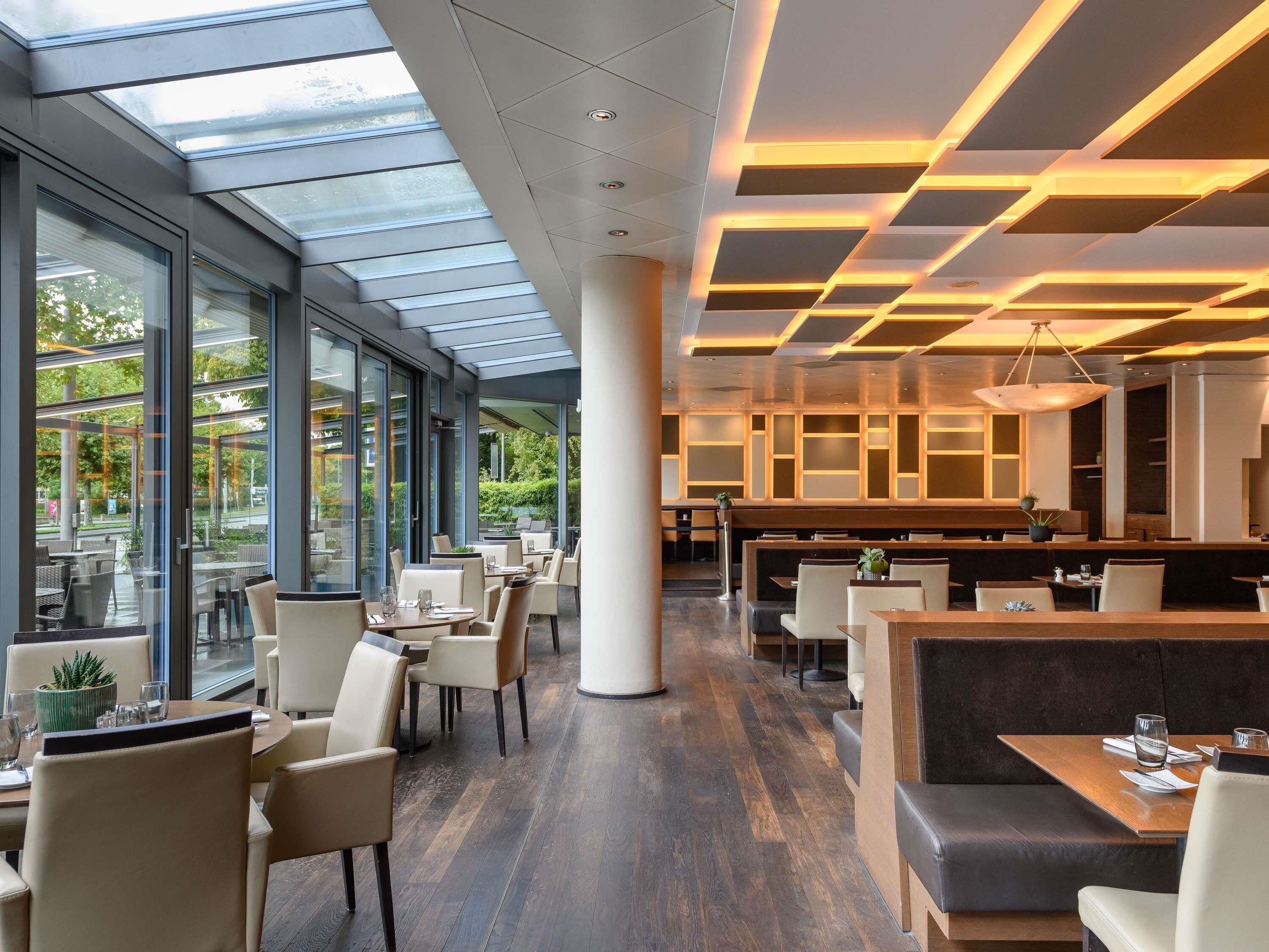 Restaurante moderno com paredes de vidro, piso de madeira e uma coluna central.