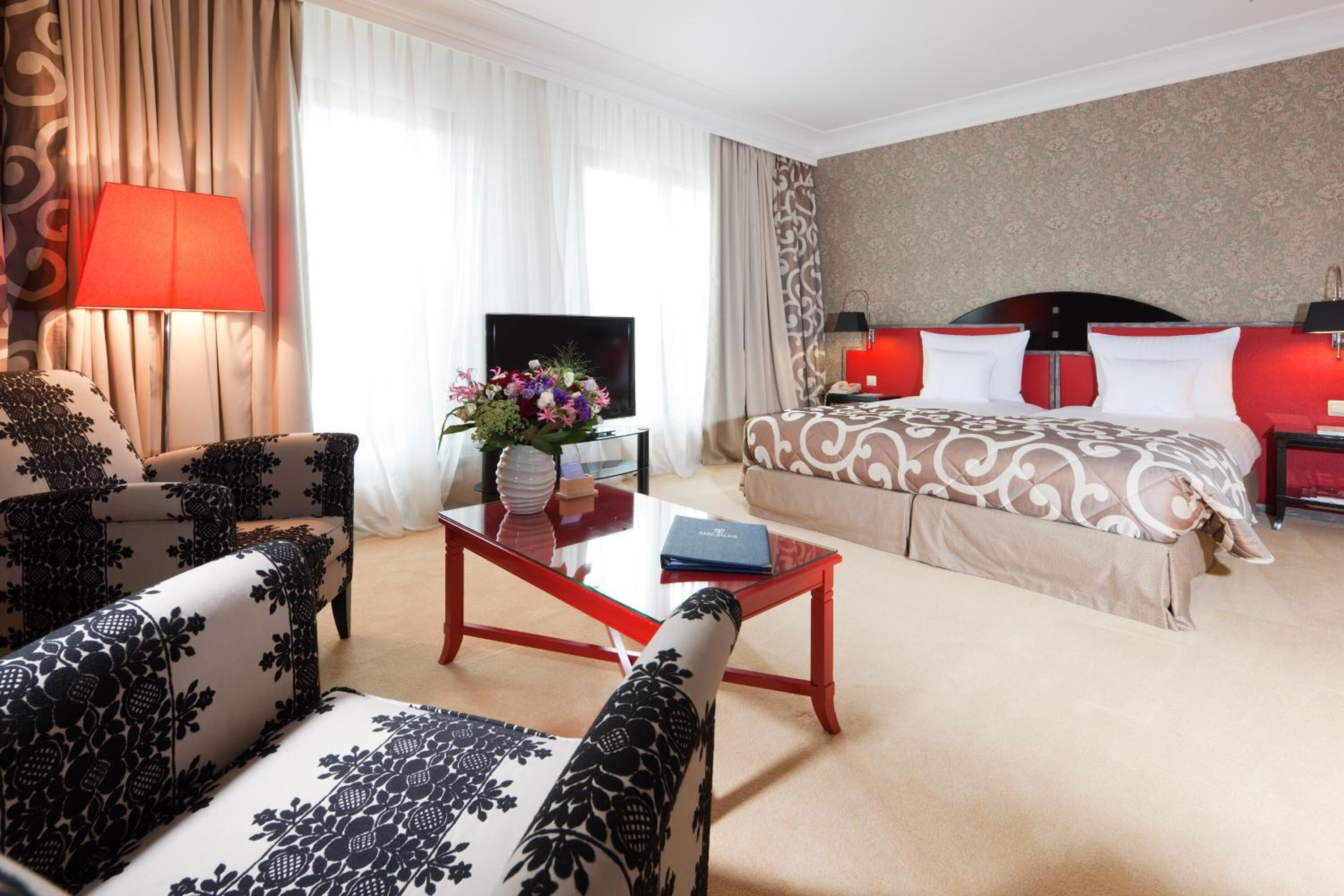 Quarto de hotel com uma cama, duas poltronas, uma mesa de centro, uma televisão e um abajur.