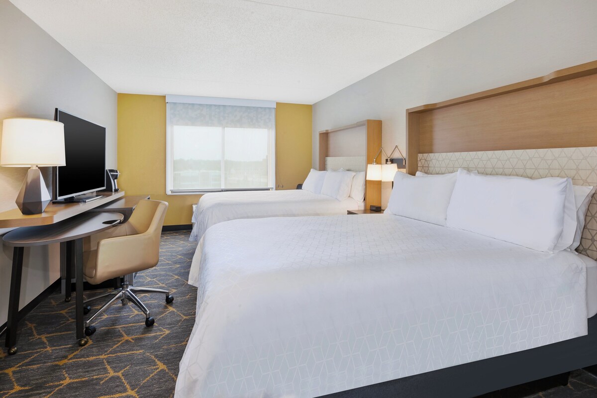Quarto de hotel com duas camas, uma secretária com televisão, uma cadeira e uma janela.