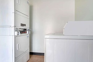 Uma lavanderia com máquinas de lavar e secar empilhadas, um painel de controle e piso revestido de azulejos.