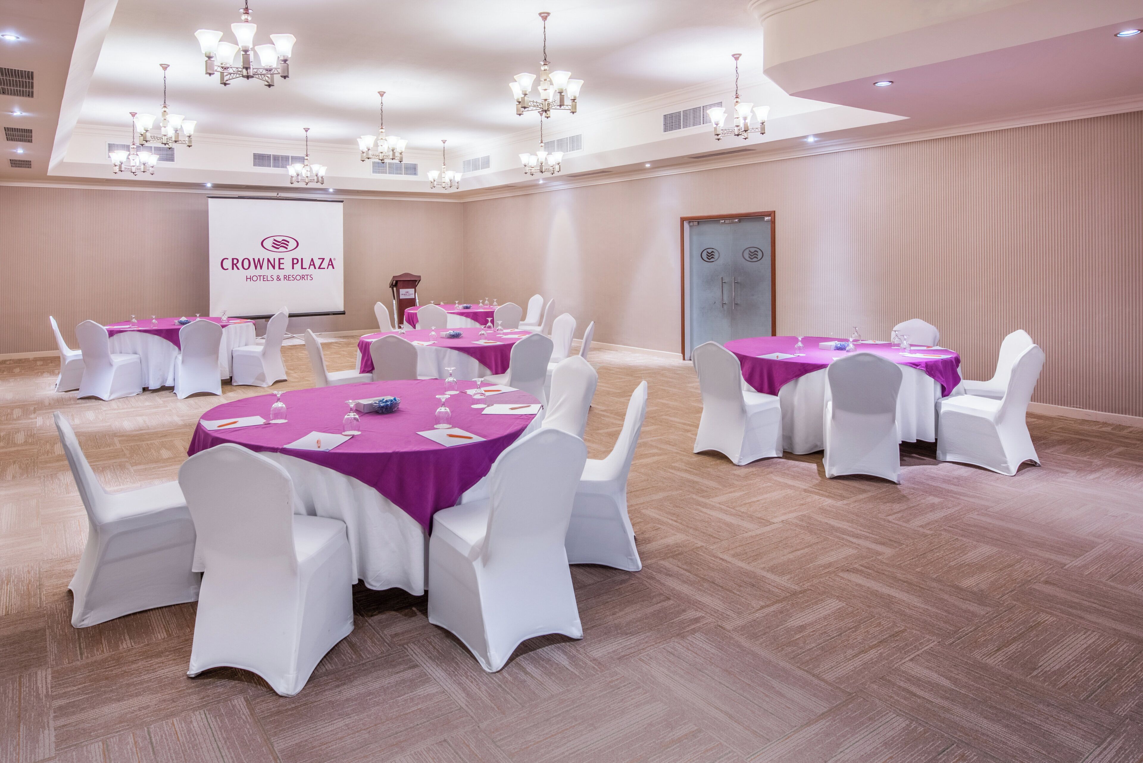 Uma sala de conferências com mesas redondas, cadeiras brancas e toalhas de mesa roxas.