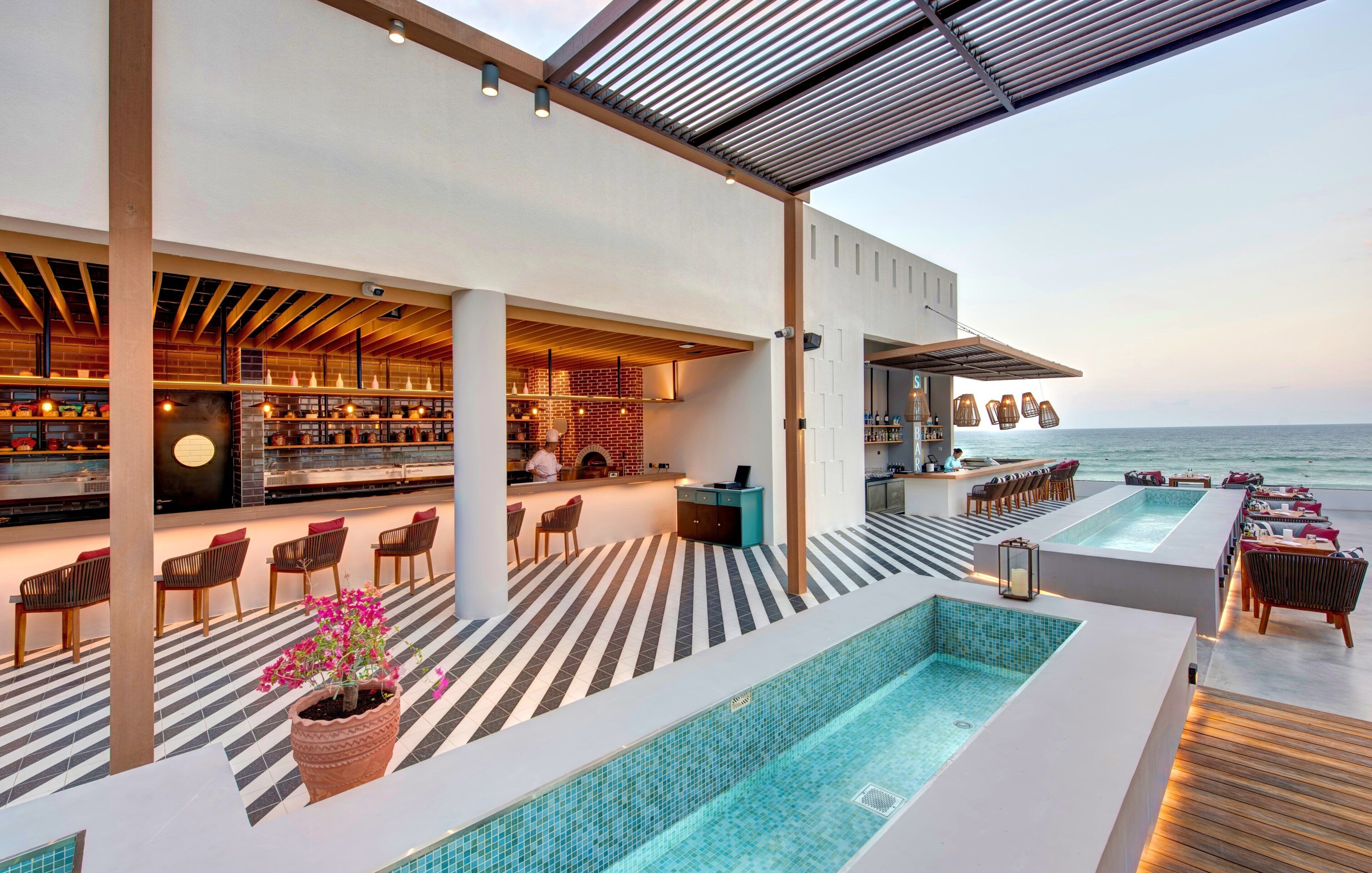Um bar no terraço com piscina, assentos e vista para o mar.