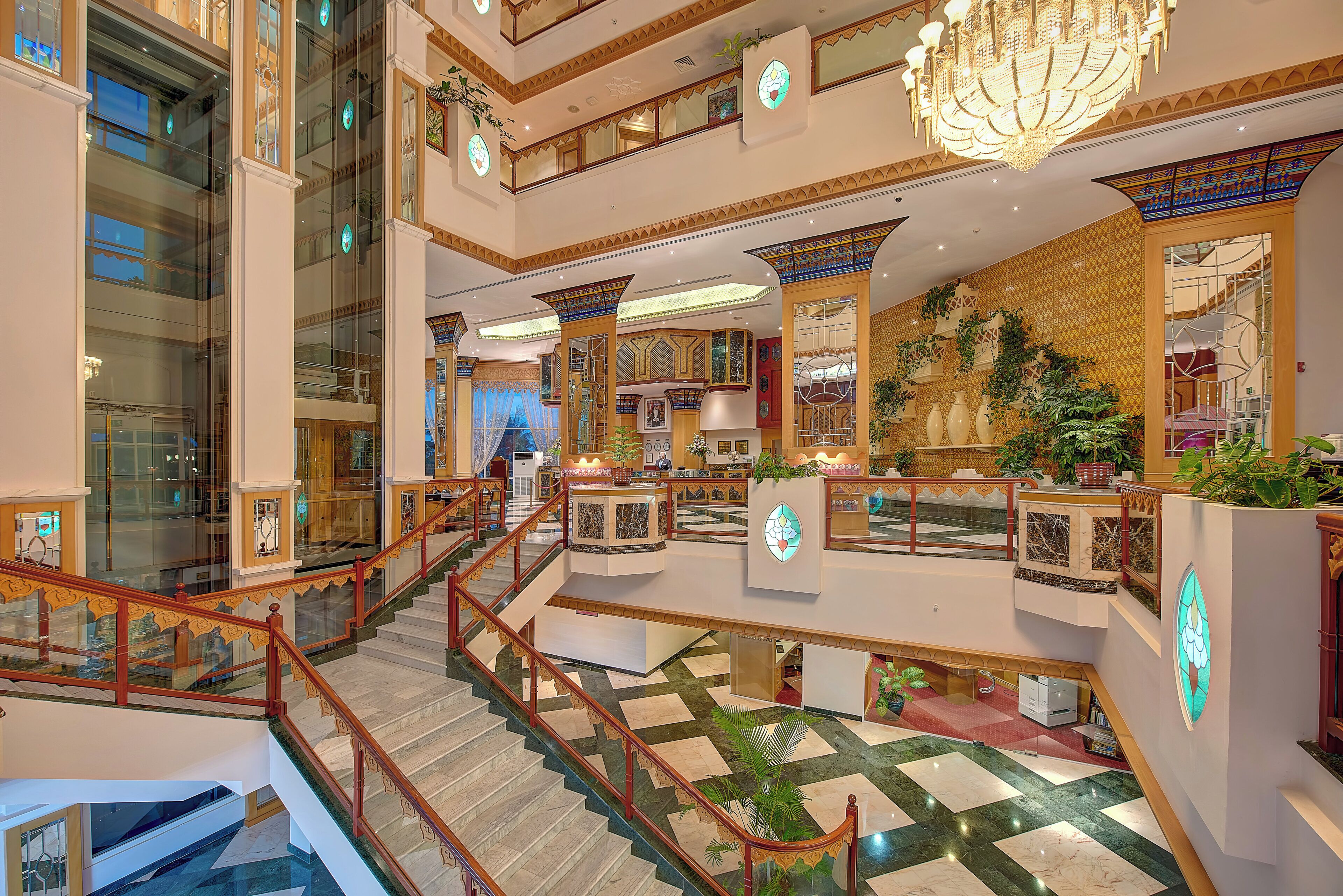 Um hall de hotel em vários níveis, com uma escadaria imponente, iluminação decorativa e um balcão de recepção.