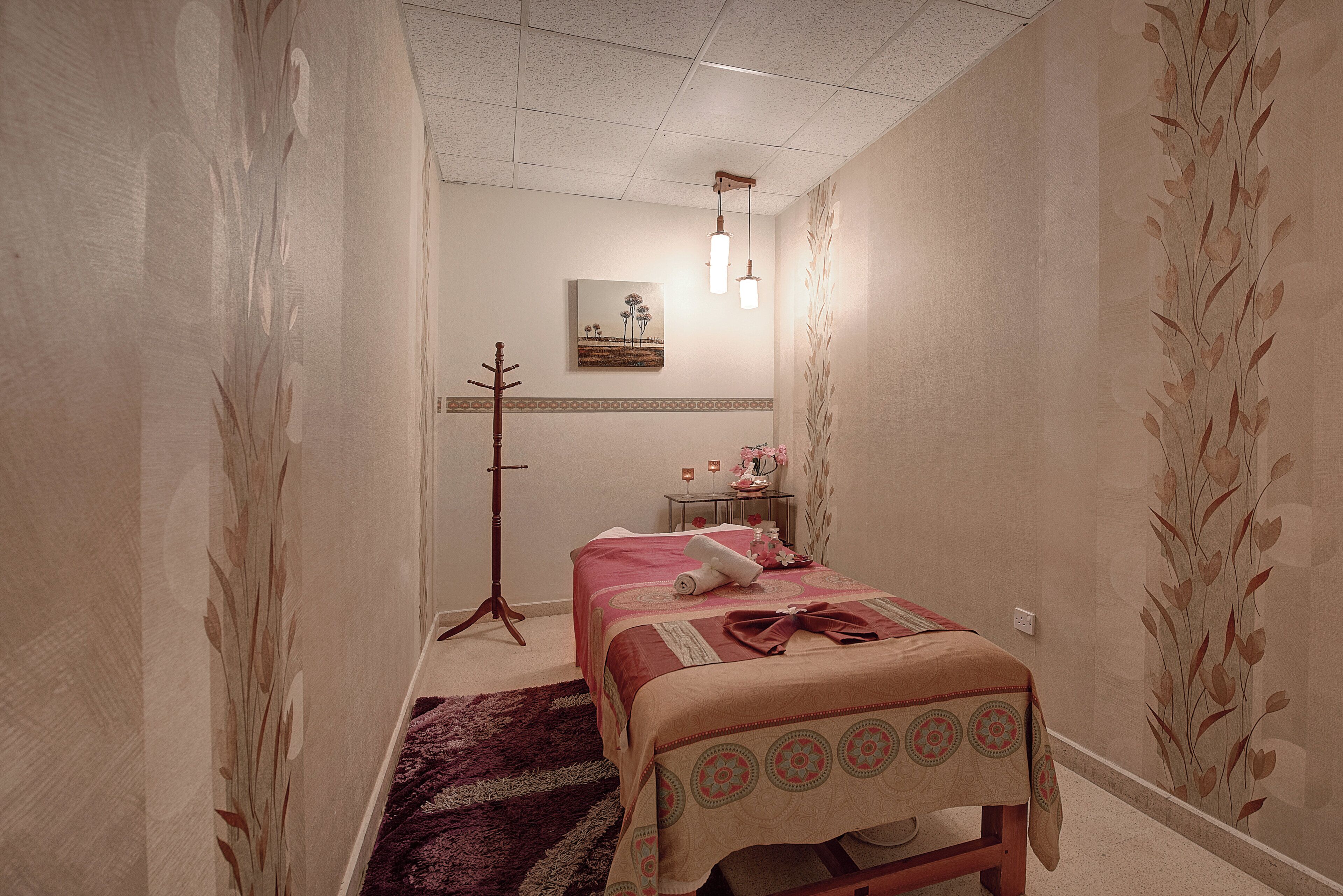 Quarto com cama, porta-casacos, uma pequena mesa com um vaso de flores e um quadro na parede.