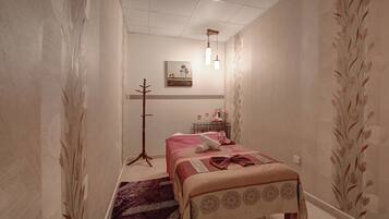 Quarto com cama, porta-casacos, uma pequena mesa com um vaso de flores e um quadro na parede.