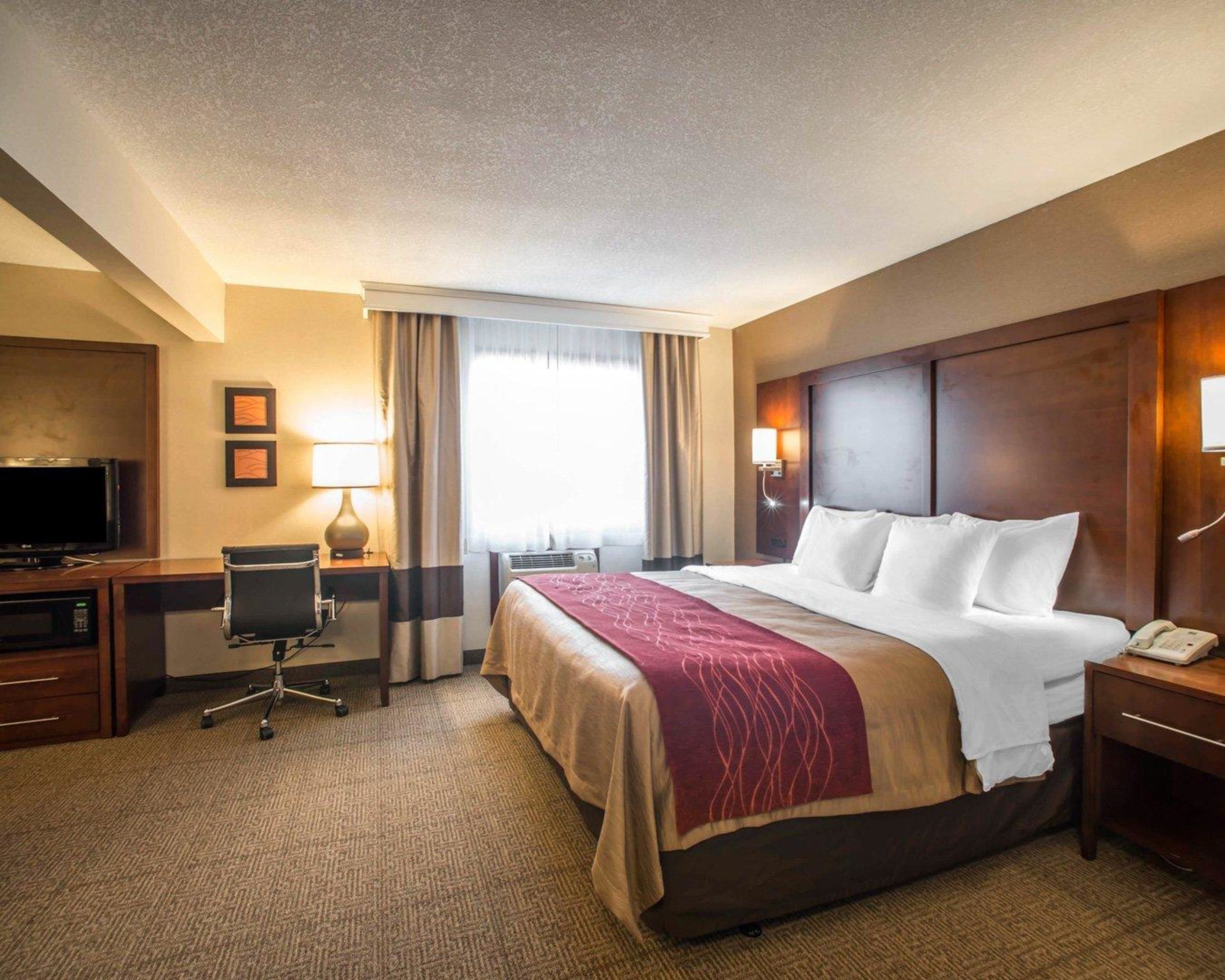 Quarto de hotel com uma cama grande, uma escrivaninha com televisão, uma cadeira, abajur e telefone.