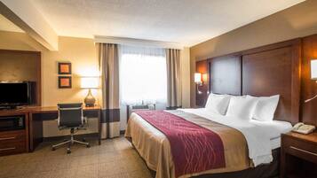 Quarto de hotel com uma cama grande, uma escrivaninha com televisão, uma cadeira, abajur e telefone.