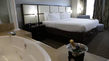 Quarto de hotel com uma cama grande, uma mesa de cabeceira, um armário para guardar objetos pessoais, banheiro com banheira e um copo de bebida.
