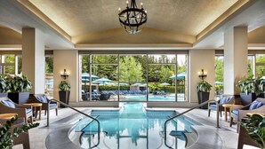 Uma área de piscina com espreguiçadeiras e guarda-sóis, janelas amplas e um candelabro.