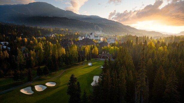 Um campo de golfe com bunkers e uma cidade ao fundo.