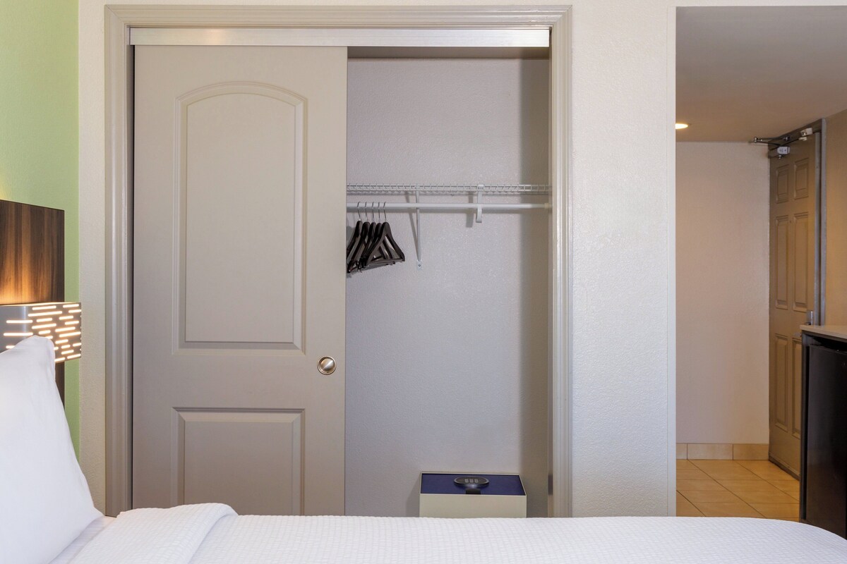 Quarto de hotel com cama, mesa de cabeceira, guarda-roupa e cabideiro.