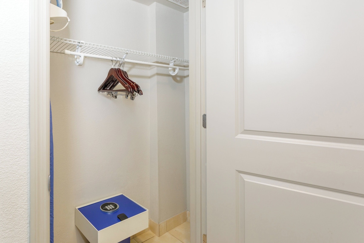 Um corredor estreito e pequeno com uma porta branca, uma prateleira branca com roupas penduradas e um armário azul com fechadura.