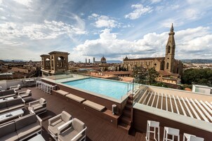 Uma área de piscina no terraço com espreguiçadeiras e vista para uma igreja histórica e paisagem urbana.