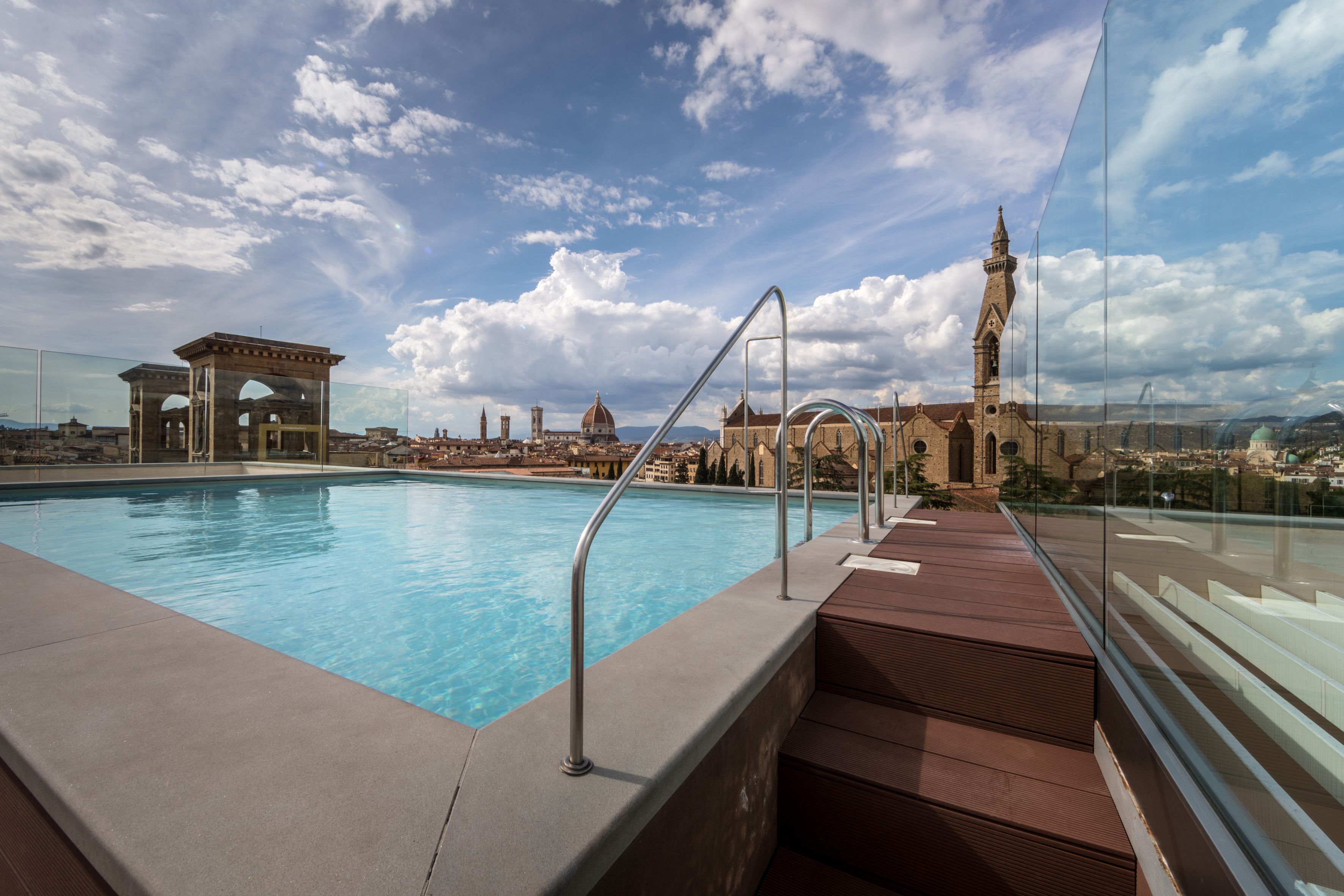 Piscina no terraço com vista clara para edifícios históricos e uma torre ao fundo.