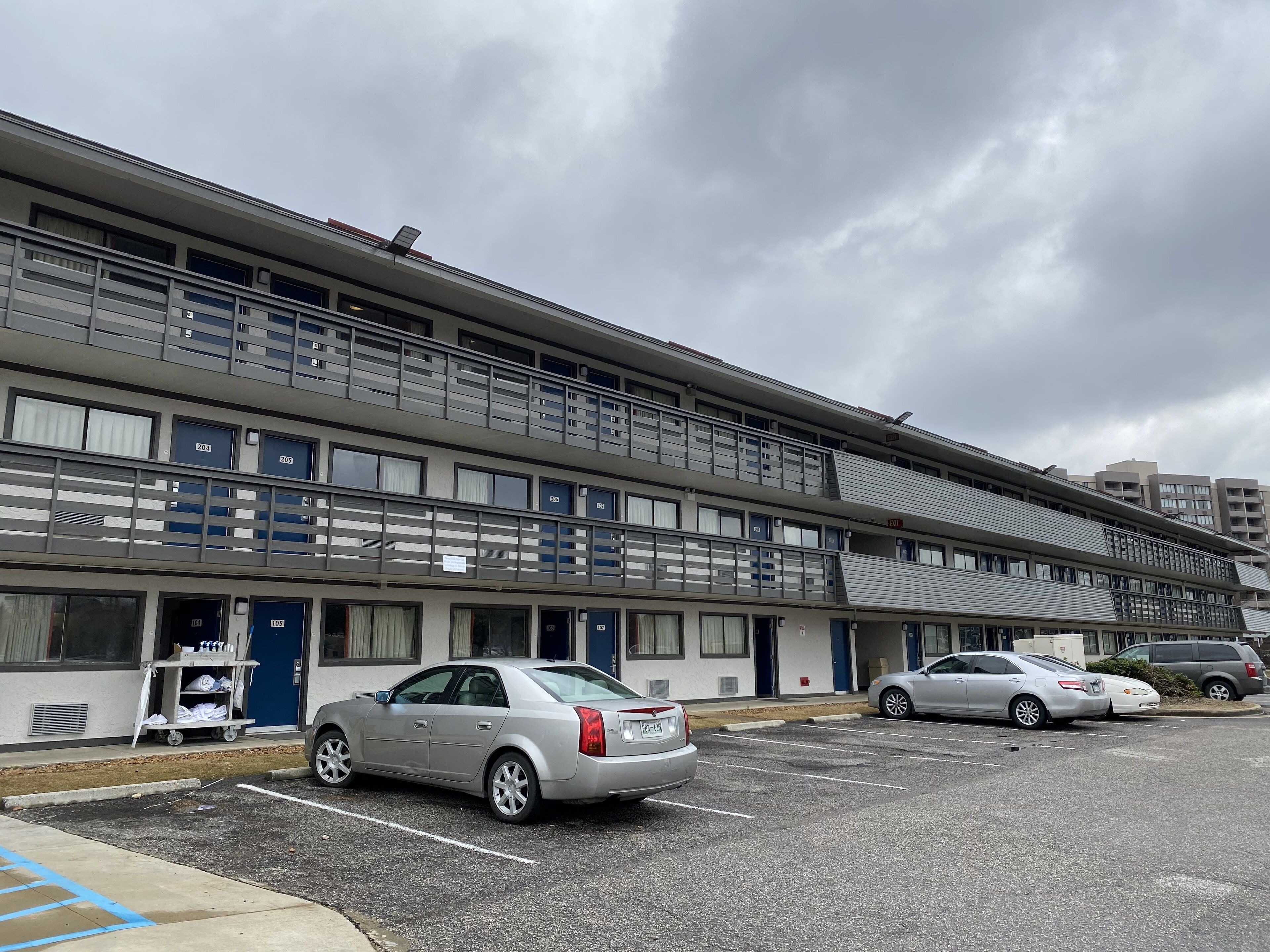 Hotel com vários andares, varandas, espaços de estacionamento e céu claro.